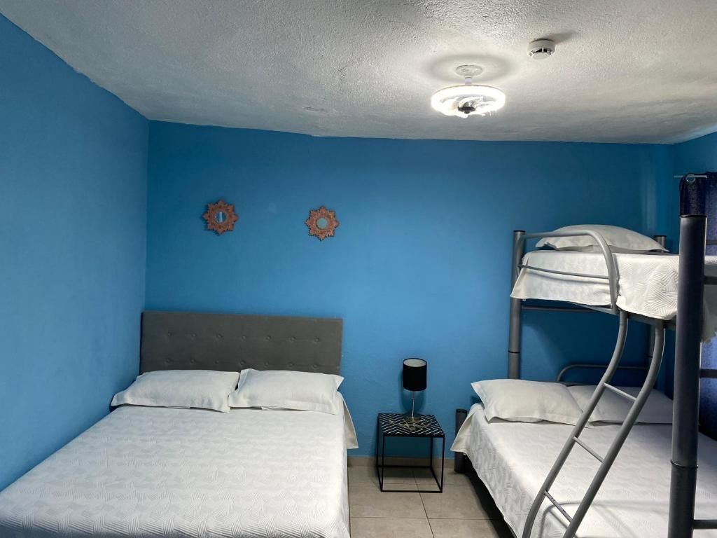 Quarto com duas camas, uma cama beliche e uma pequena mesa com luminária.