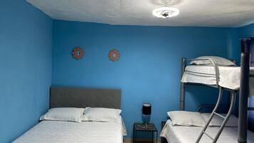 Quarto com duas camas, uma cama beliche e uma pequena mesa com luminária.
