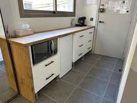Uma cozinha compacta com micro-ondas embutido, cafeteira e geladeira pequena.