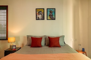 Quarto de hotel com cama, duas almofadas, mesa de cabeceira com abajur e duas obras de arte emolduradas na parede.