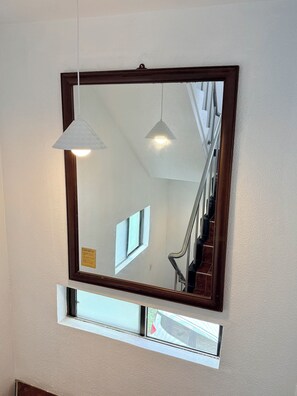 Um espelho com moldura de madeira, uma luminária pendente e uma janela abaixo.