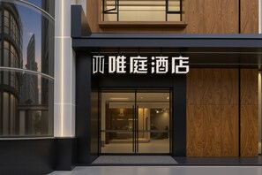 Entrada de hotel com design moderno, exibindo uma grande placa iluminada acima da porta.