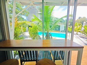 Quarto com vista para uma piscina, rodeado por vegetação e um edifício alto.