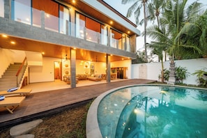 Uma casa moderna de dois andares com piscina, deck de madeira e escada que leva ao andar superior.