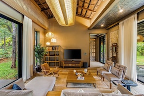 Uma sala de estar ampla com uma grande TV de tela plana, assentos confortáveis e vista para o exterior.
