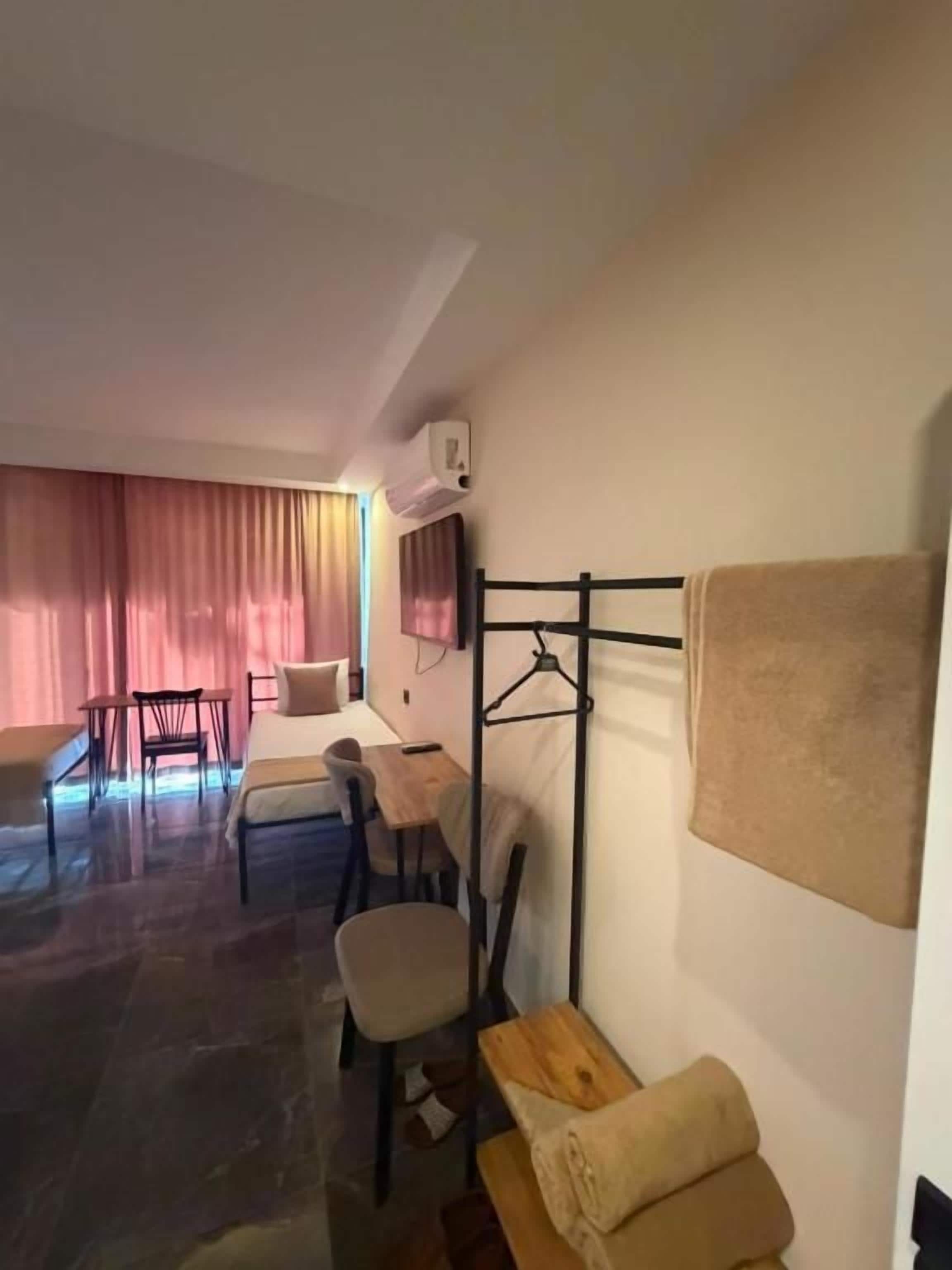 Quarto de hotel com cama, escrivaninha, cadeira, porta-roupas e janela com cortinas.
