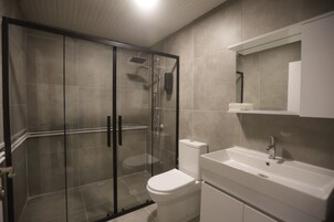 Casa de banho moderna com cabine de duche em vidro, sanita branca e lavatório com espelho.
