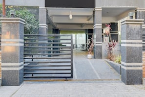 Uma entrada com portão fechado, caminho pavimentado e um vaso de planta à direita.