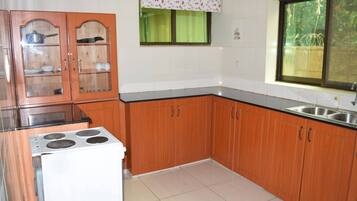 Cozinha com armários de madeira, geladeira branca, fogão e janela com cortina verde.