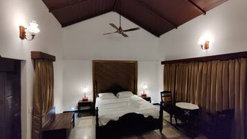 Quarto de hotel com cama, escrivaninha, cadeira, ventoinha no teto e duas luminárias de parede.