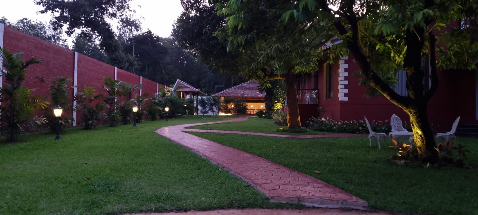 Uma trilha leva a um edifício com fachada vermelha, cercado por vegetação e árvores.