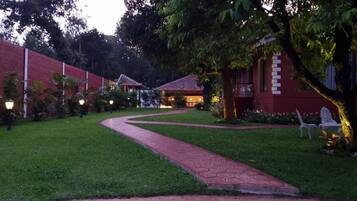 Uma trilha leva a um edifício com fachada vermelha, cercado por vegetação e árvores.