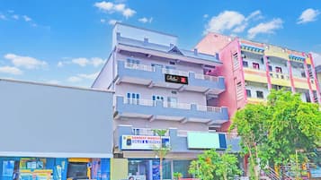Um edifício com vários andares e diversos estabelecimentos comerciais no andar térreo, incluindo uma farmácia e uma assistência técnica móvel.