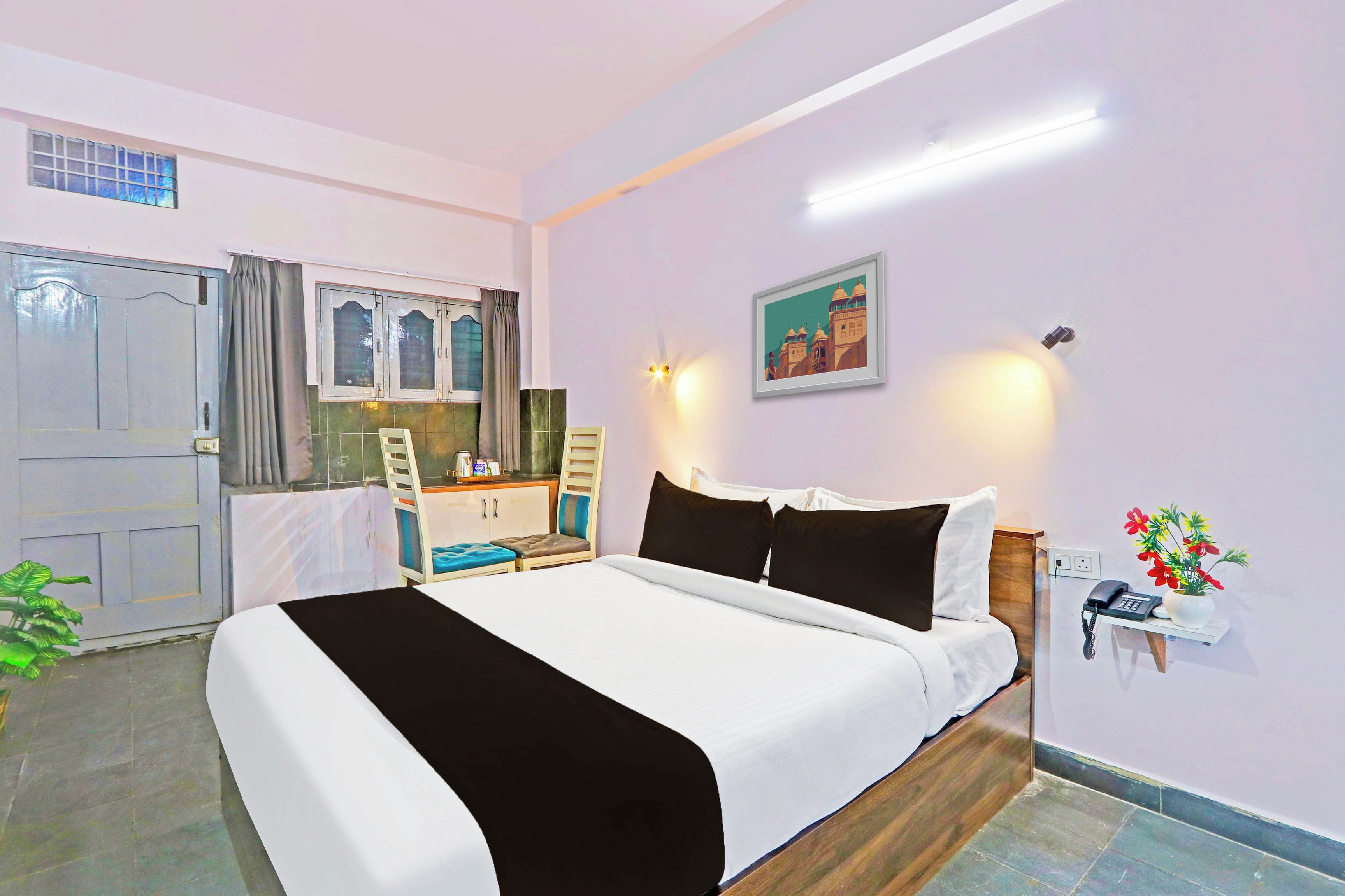 Quarto de hotel com cama, escrivaninha, cadeira, pequena mesa com um vaso de flores e um quadro na parede.
