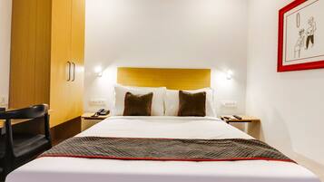 Quarto de hotel com cama, mesas de cabeceira, escrivaninha, cadeira e uma obra de arte na parede.
