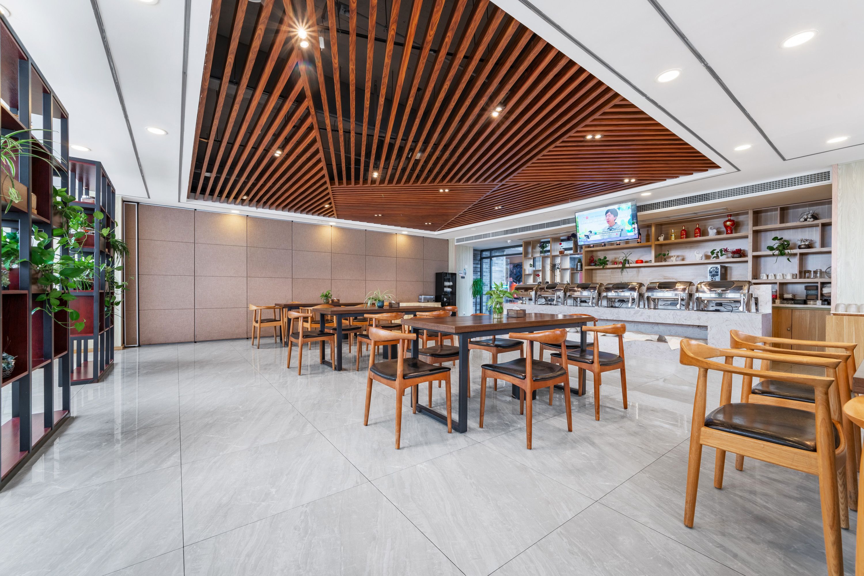Uma sala de jantar moderna com mesas e cadeiras de madeira, uma tela de televisão e prateleiras com diversos objetos.