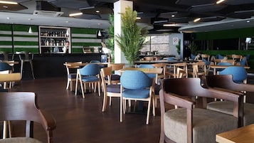 Um restaurante moderno com mesas e cadeiras de madeira, área de bar e uma parede verde.