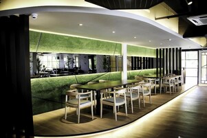Um restaurante moderno com área de estar curvada, parede verde e uma longa mesa de madeira.