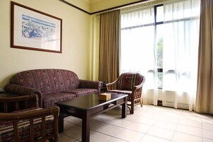 Uma sala de estar com sofá, poltronas, mesa de centro e uma janela grande com cortinas.