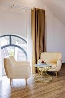 Quarto com duas poltronas, uma mesa redonda e uma janela com cortinas.