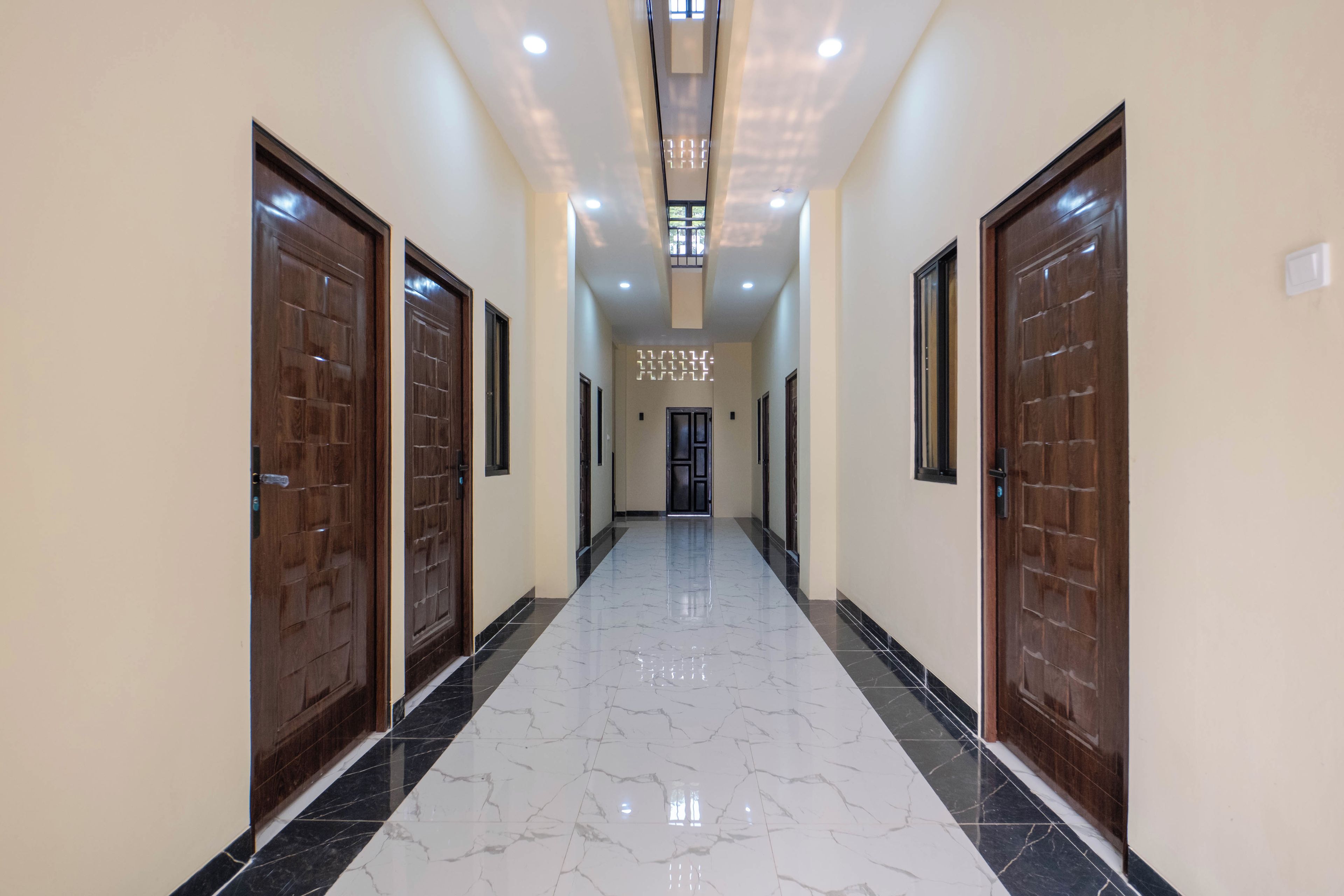 Um corredor com portas de madeira em ambos os lados, que leva a um quarto com uma placa sobre a porta.