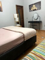 Quarto com cama, cadeira, escrivaninha e espelho.