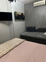 Quarto com cama, televisão de tela plana na parede, um quadro e parede listrada.