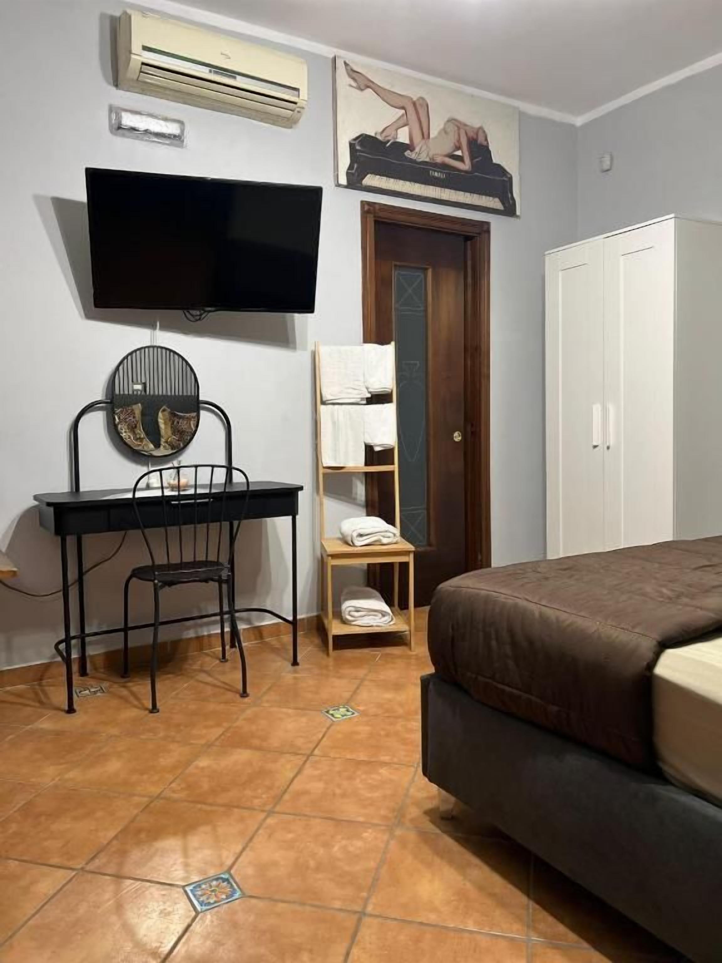 Quarto com cama, escrivaninha, cadeira, televisão, guarda-roupa e porta.
