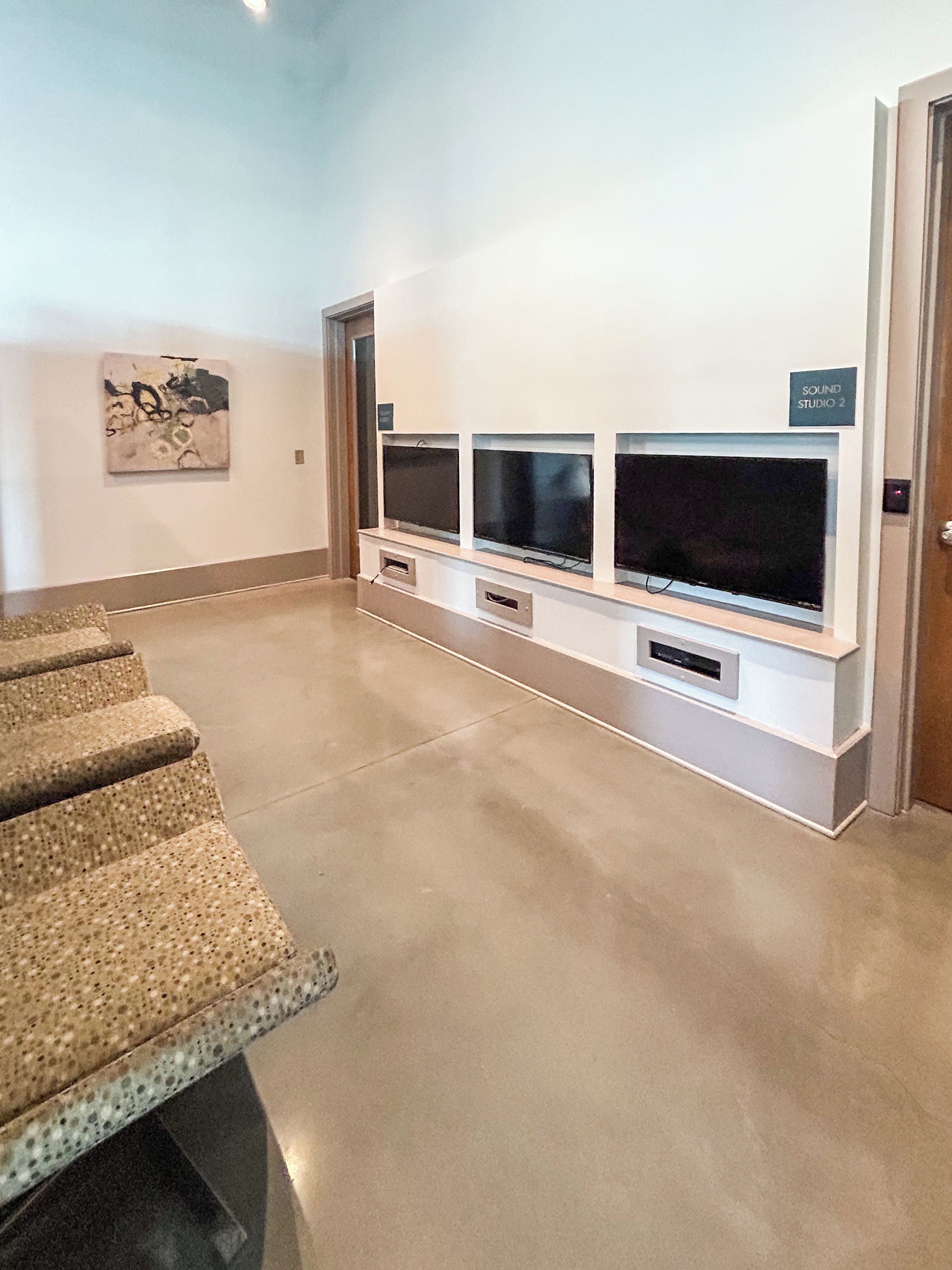 Quarto com área de estar, televisão fixada na parede e placa com a inscrição 'SOUND STUDIO 2'.