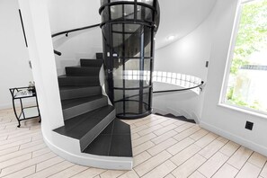 Escadaria em espiral com proteção de vidro, que dá acesso a um patamar com vista para o verde lá fora.