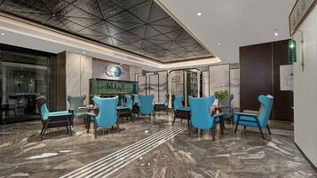 Interior moderno com design geométrico no teto, piso de mármore e cadeiras estofadas em azul dispostas em torno de uma mesa central.