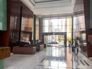 Um hall moderno com balcão de recepção, área de estar e vista para a rua através de grandes portas de vidro.