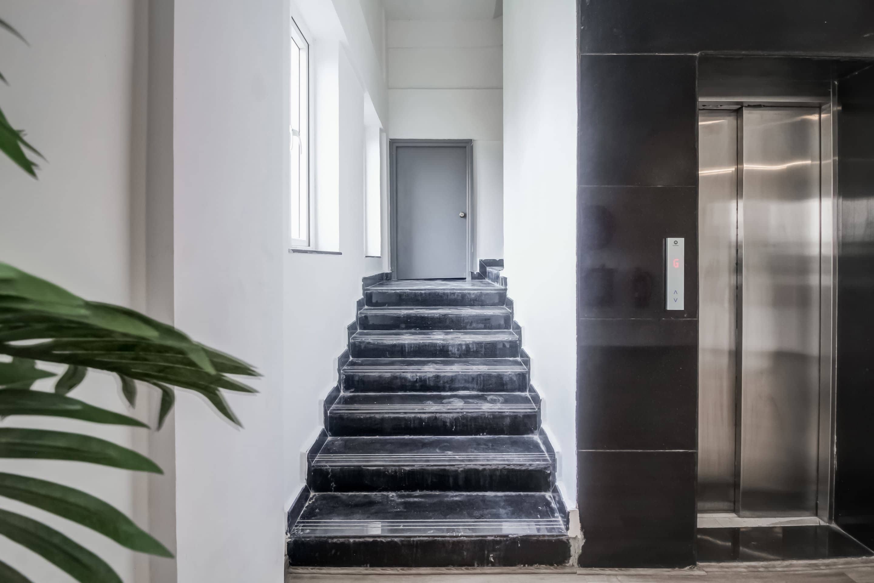 Escada que leva a uma porta, com um elevador moderno à direita.
