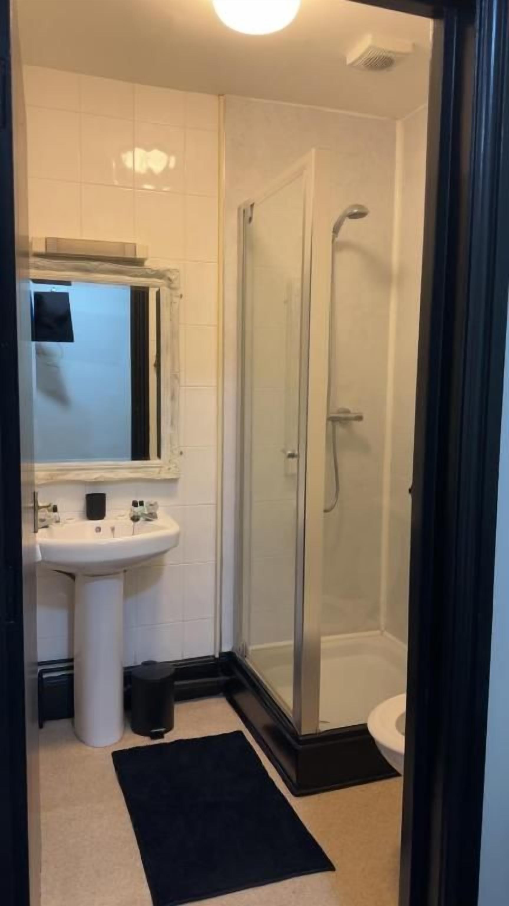 Casa de banho com chuveiro envolto em vidro, lavatório branco e sanita.