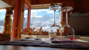Mesa com copos de vinho e vista para montanhas cobertas de neve através de uma janela.