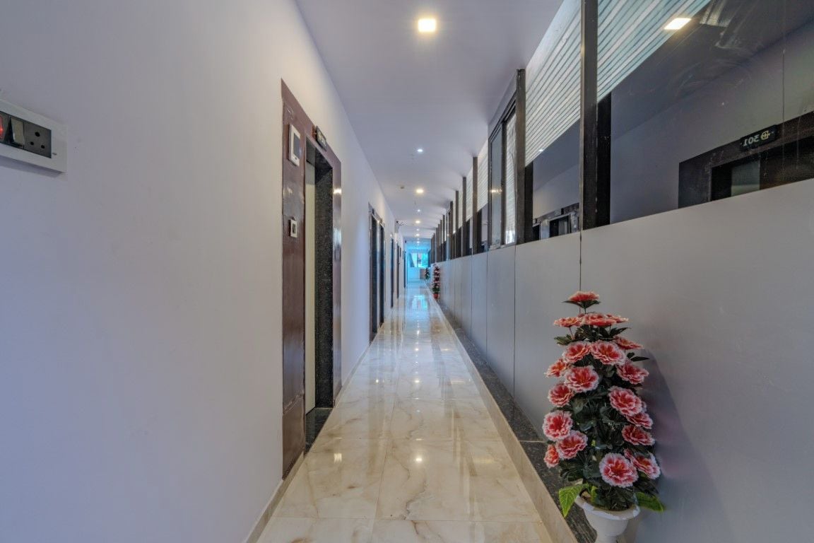 Um corredor com piso de mármore, portas à esquerda e um vaso de planta à direita.