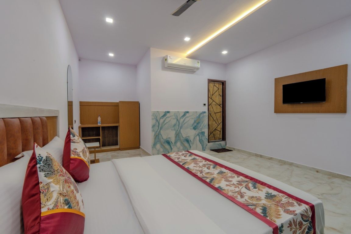 Quarto de hotel com cama, televisão fixada na parede e um pequeno espaço de estar com um armário de madeira.