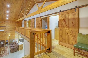 Um amplo loft com teto alto, vigas de madeira, um mezanino e uma porta de celeiro deslizante.