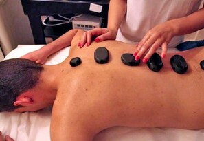 Uma pessoa recebendo massagem nas costas com pedras pretas.