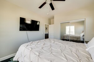 Quarto com cama, ventoinha no teto, televisão fixada na parede e porta de acesso a outro espaço.