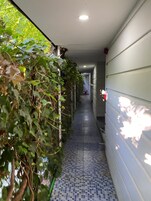 Um corredor estreito com chão de azulejos, uma parede de um lado e uma parede coberta de plantas do outro.