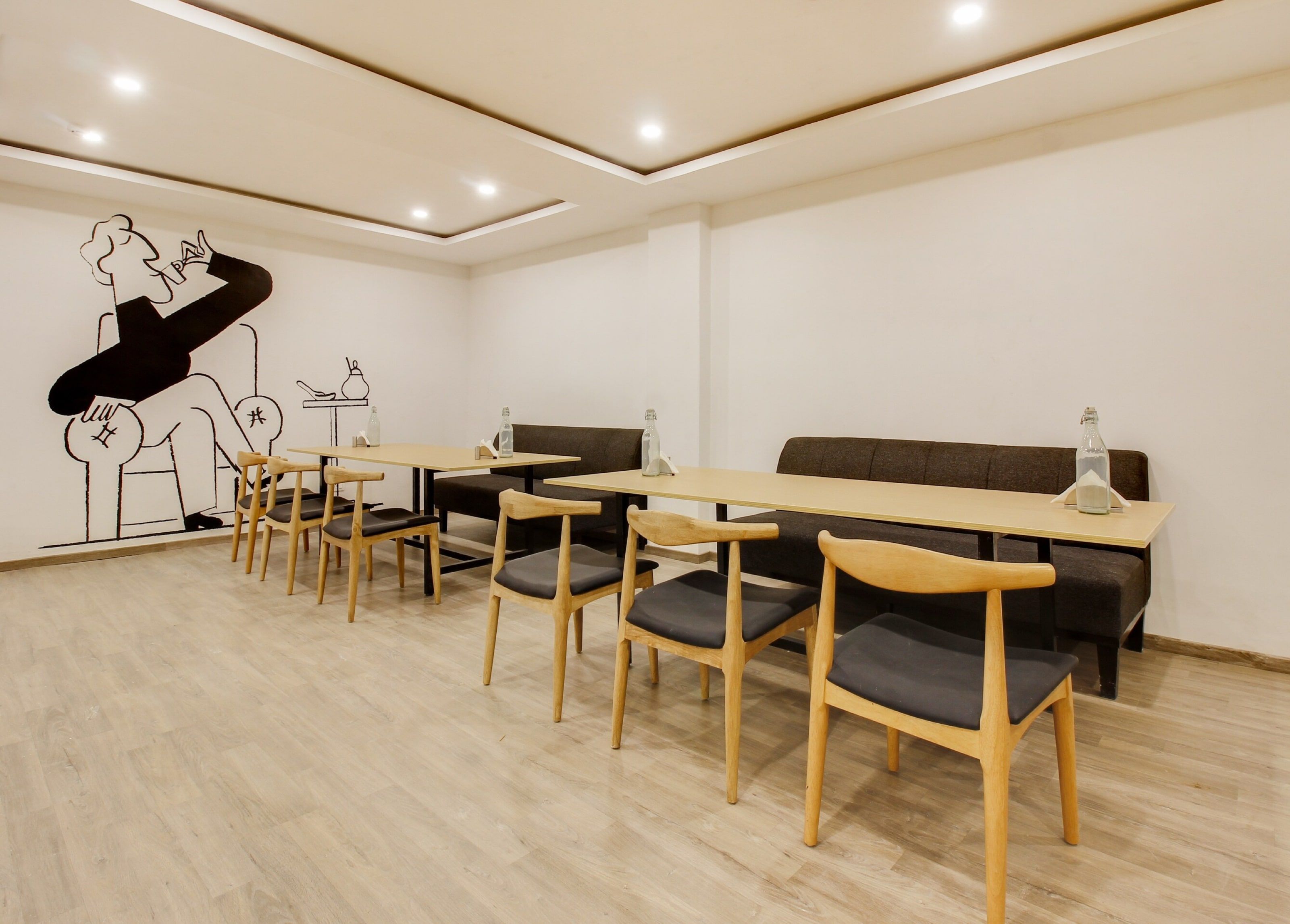 Uma sala de jantar moderna com mesas e cadeiras de madeira, um sofá preto e um mural na parede.