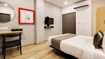 Quarto de hotel com cama, escrivaninha, cadeira, televisão e porta com tranca.