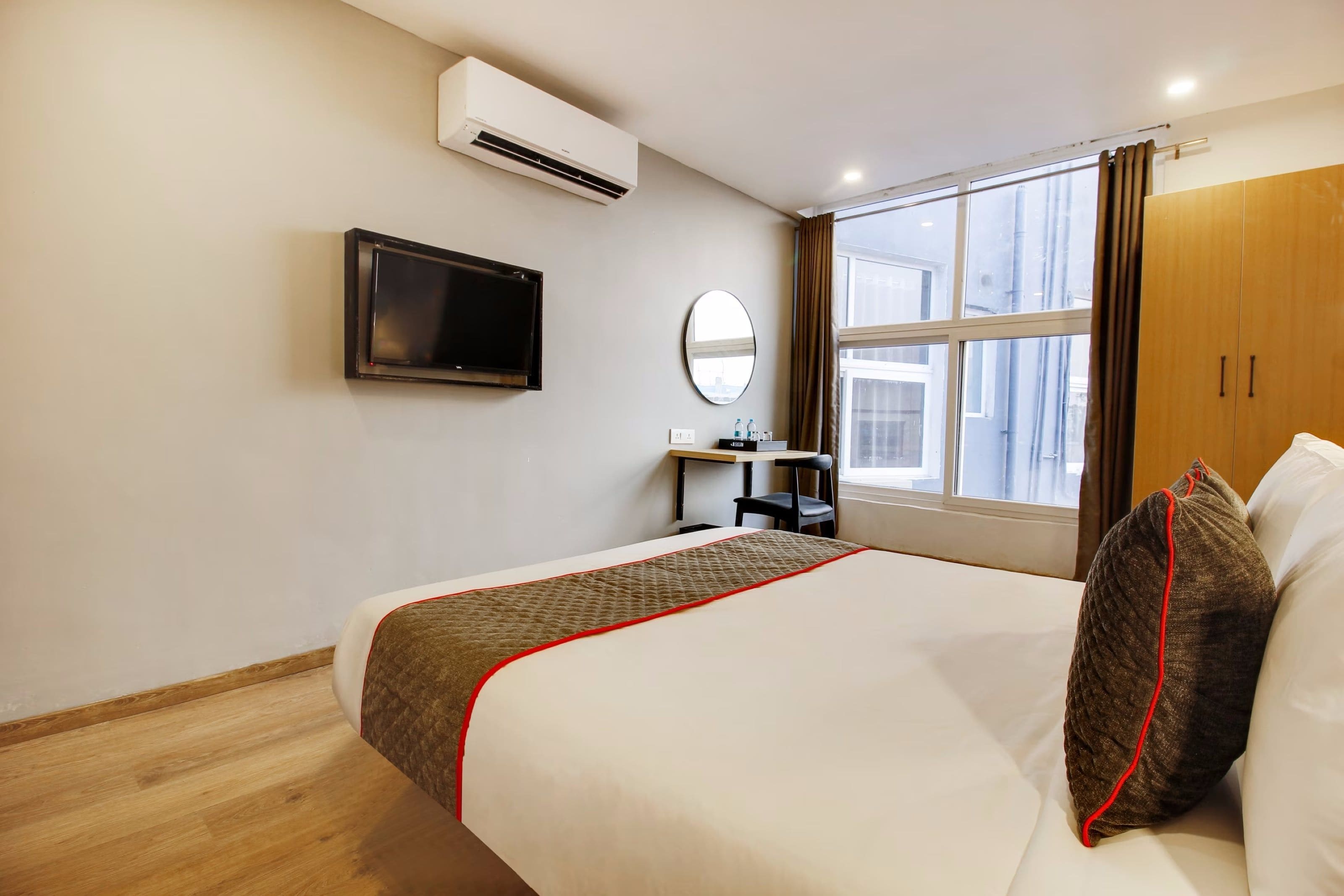 Quarto de hotel com cama, televisão de tela plana, escrivaninha com cadeira, janela com cortinas e guarda-roupa.