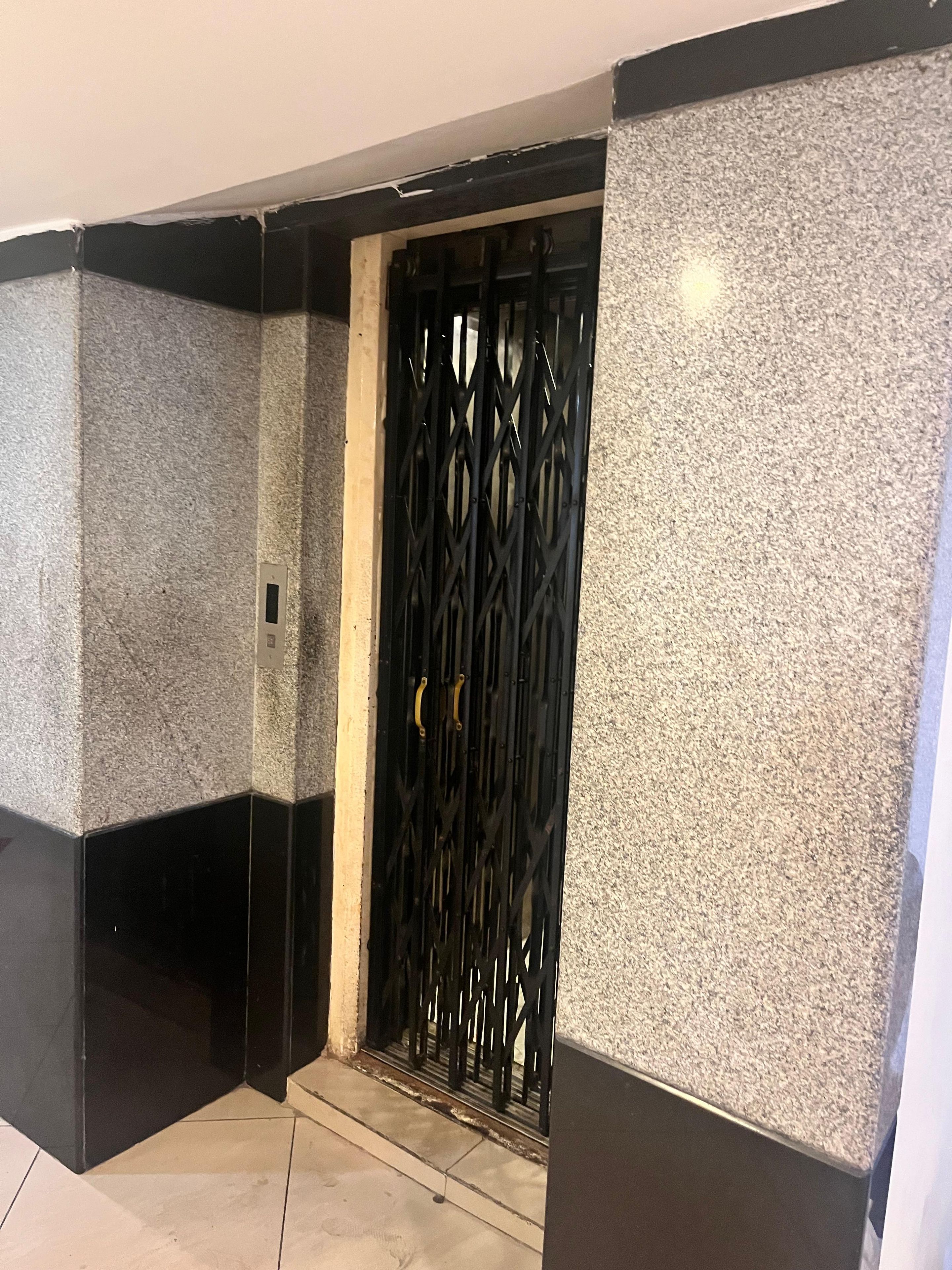 Um corredor com parede texturizada, portão de metal preto e chão de azulejos.