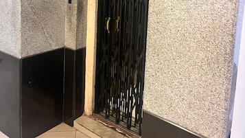 Um corredor com parede texturizada, portão de metal preto e chão de azulejos.