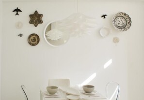 Uma área de jantar com uma mesa posta para dois, um espelho e decorações nas paredes, incluindo uma estrela, um pássaro e um prato com design floral.