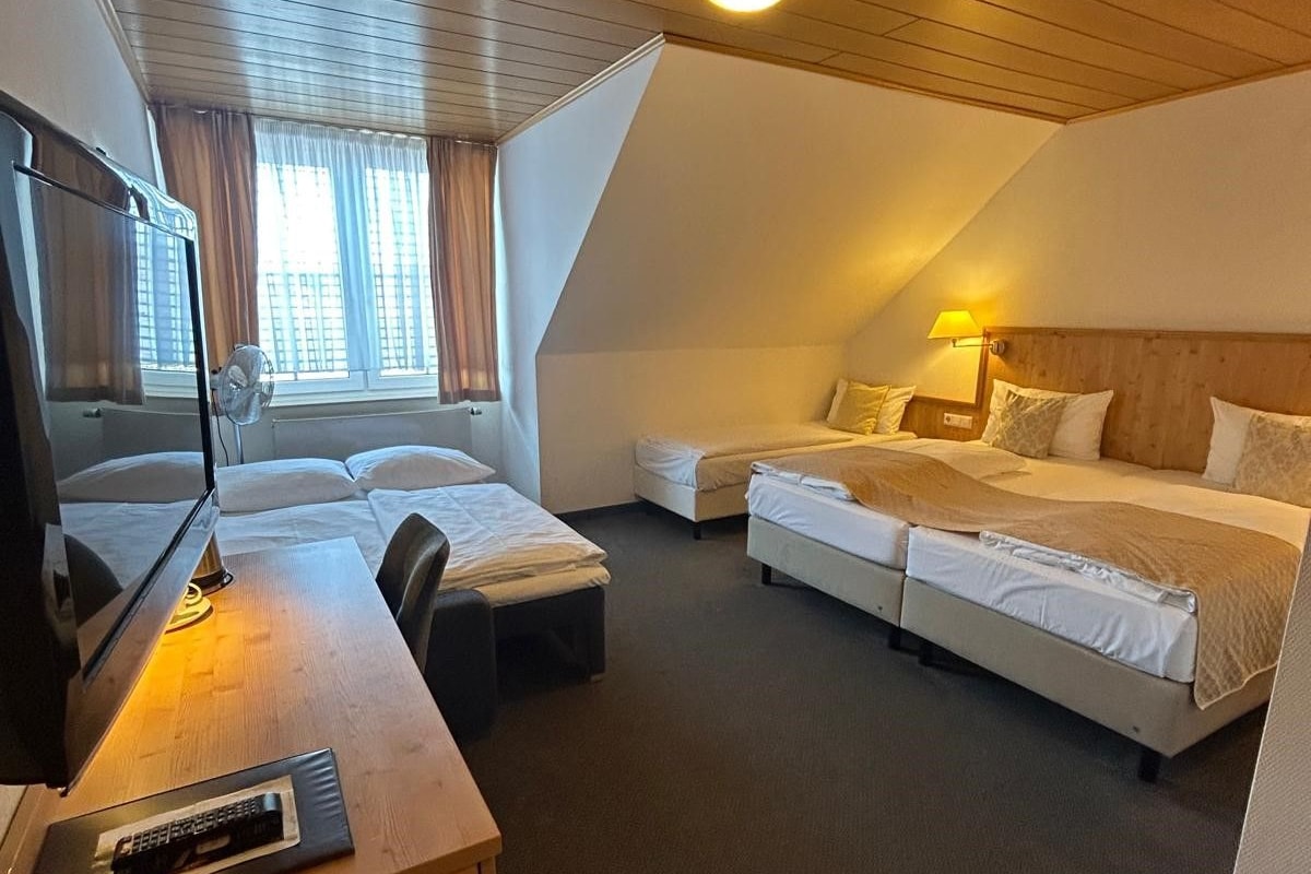 Quarto de hotel com teto de madeira, uma mesa com televisão, duas camas e uma janela com cortinas.