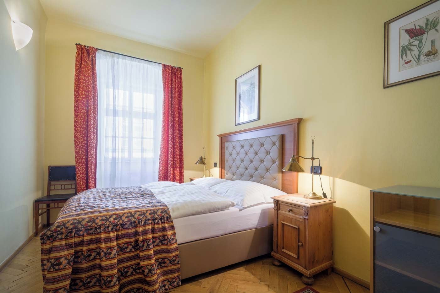 Quarto com cama, mesa de cabeceira, luminária, cadeira e janela com cortinas.