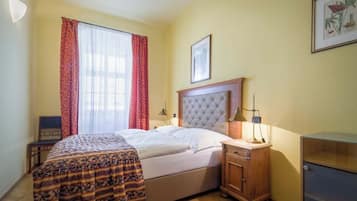 Quarto com cama, mesa de cabeceira, luminária, cadeira e janela com cortinas.